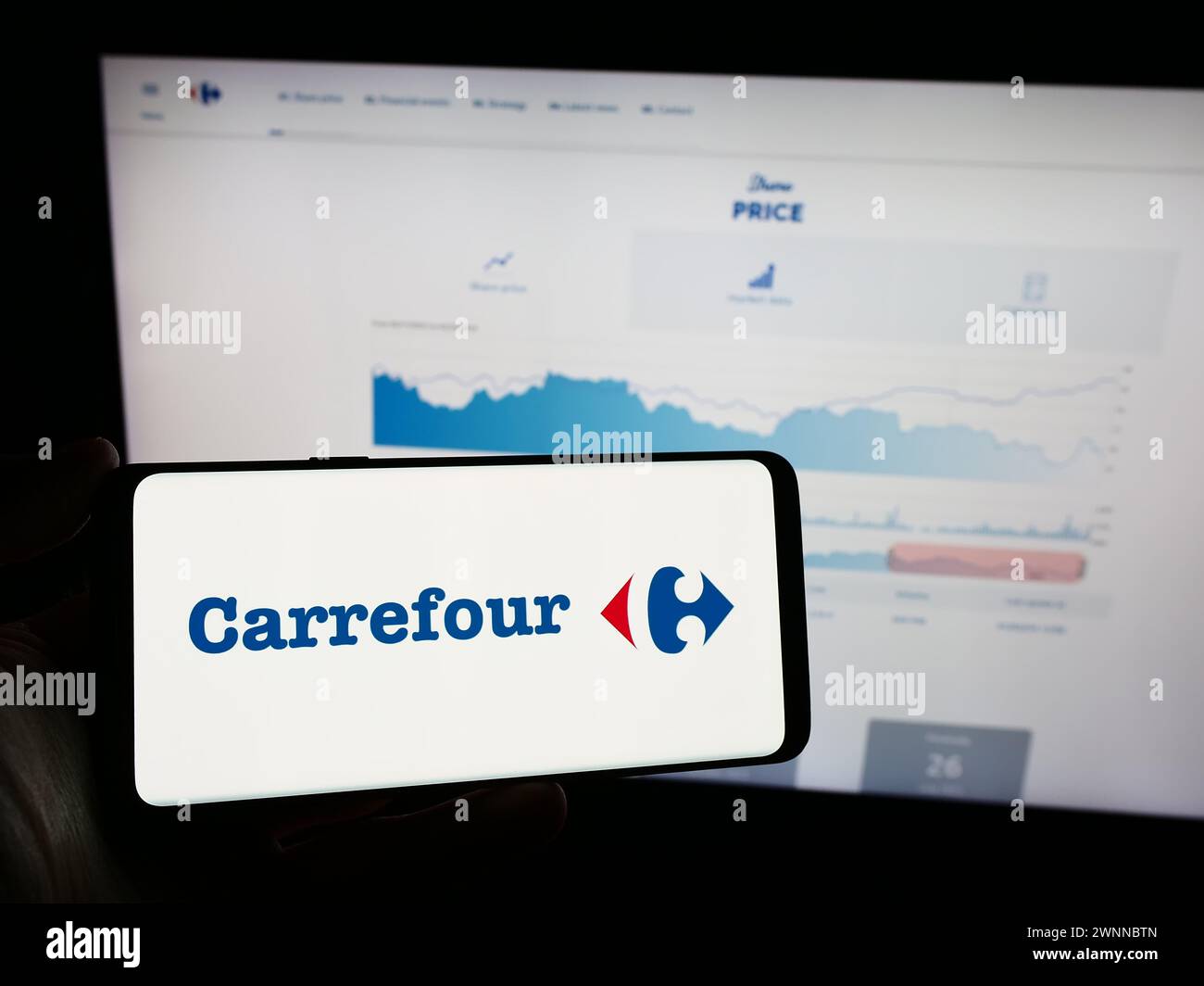 Person holding mobile phone with logo of French retail company Carrefour S.A. in front of ...
