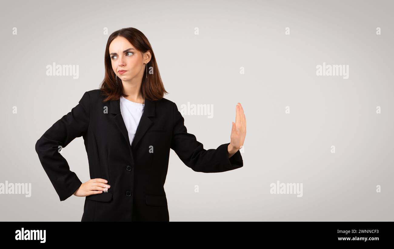 Distrustful businesswoman in a black suit jacket showing a stop hand ...