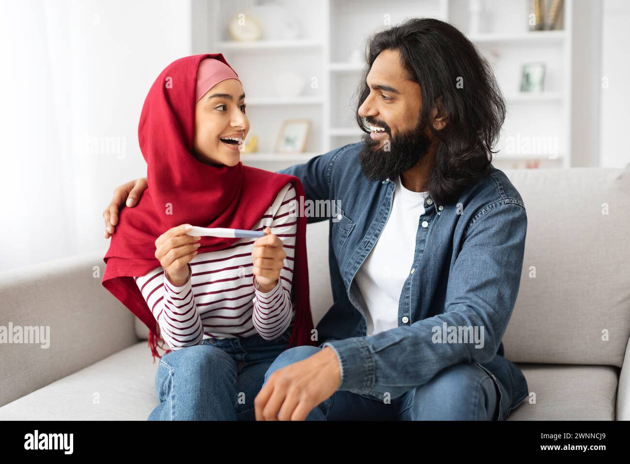 Happy Muslim Couple Holding Positive Pregnancy Test And Looking At Each ...