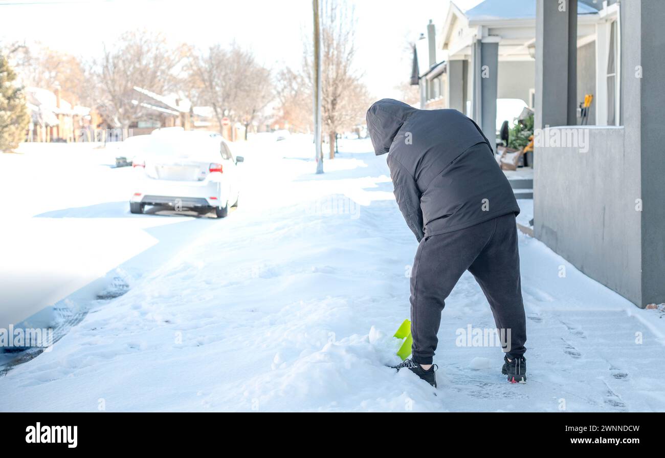 A man in a warm black jacket and trousers shoveling snow in front of ...