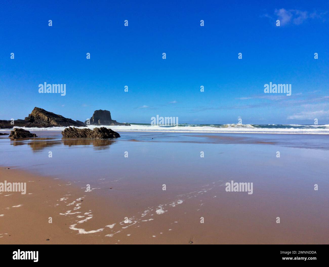 Ocean waves meet a sandy shore under a bright sky, with an imposing ...