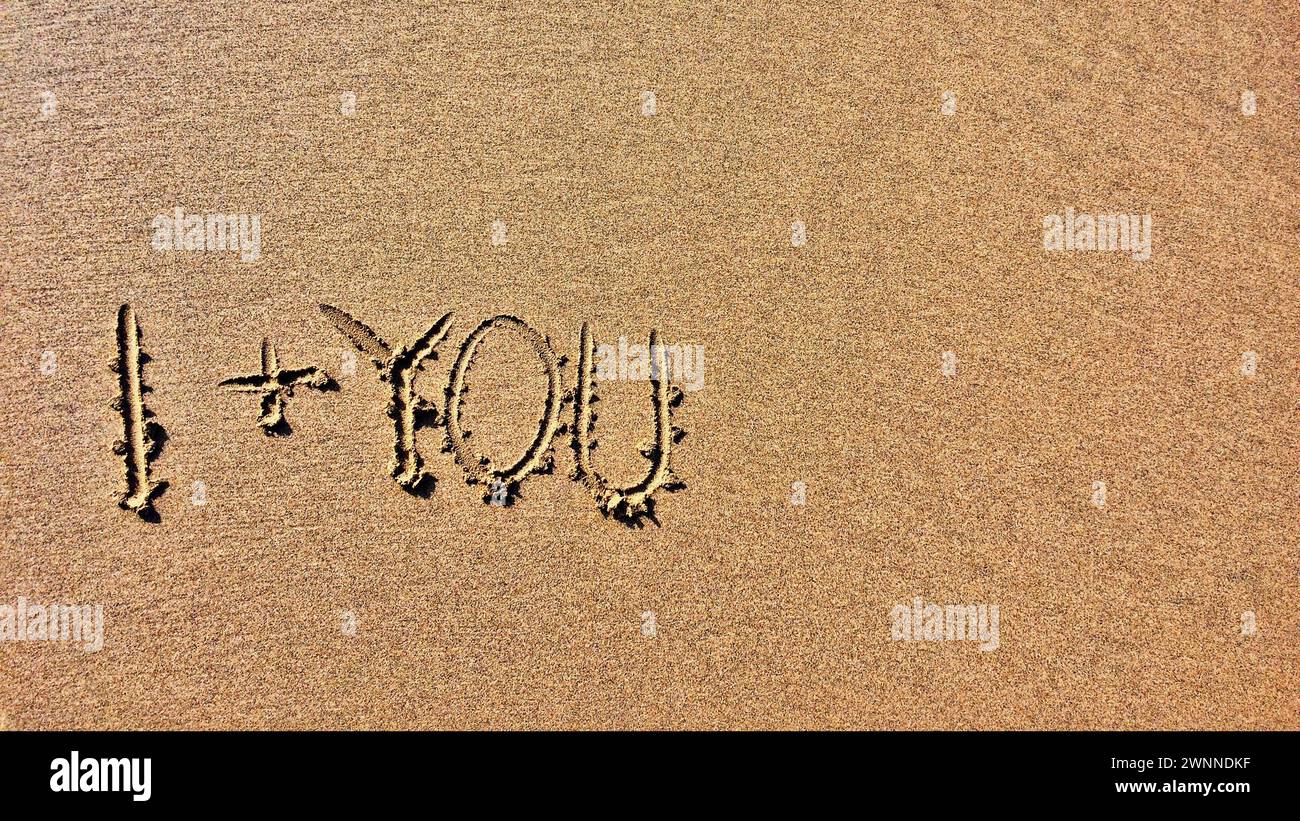 A sandy surface bears the inscription ‘I + YOU’, indicating a romantic ...