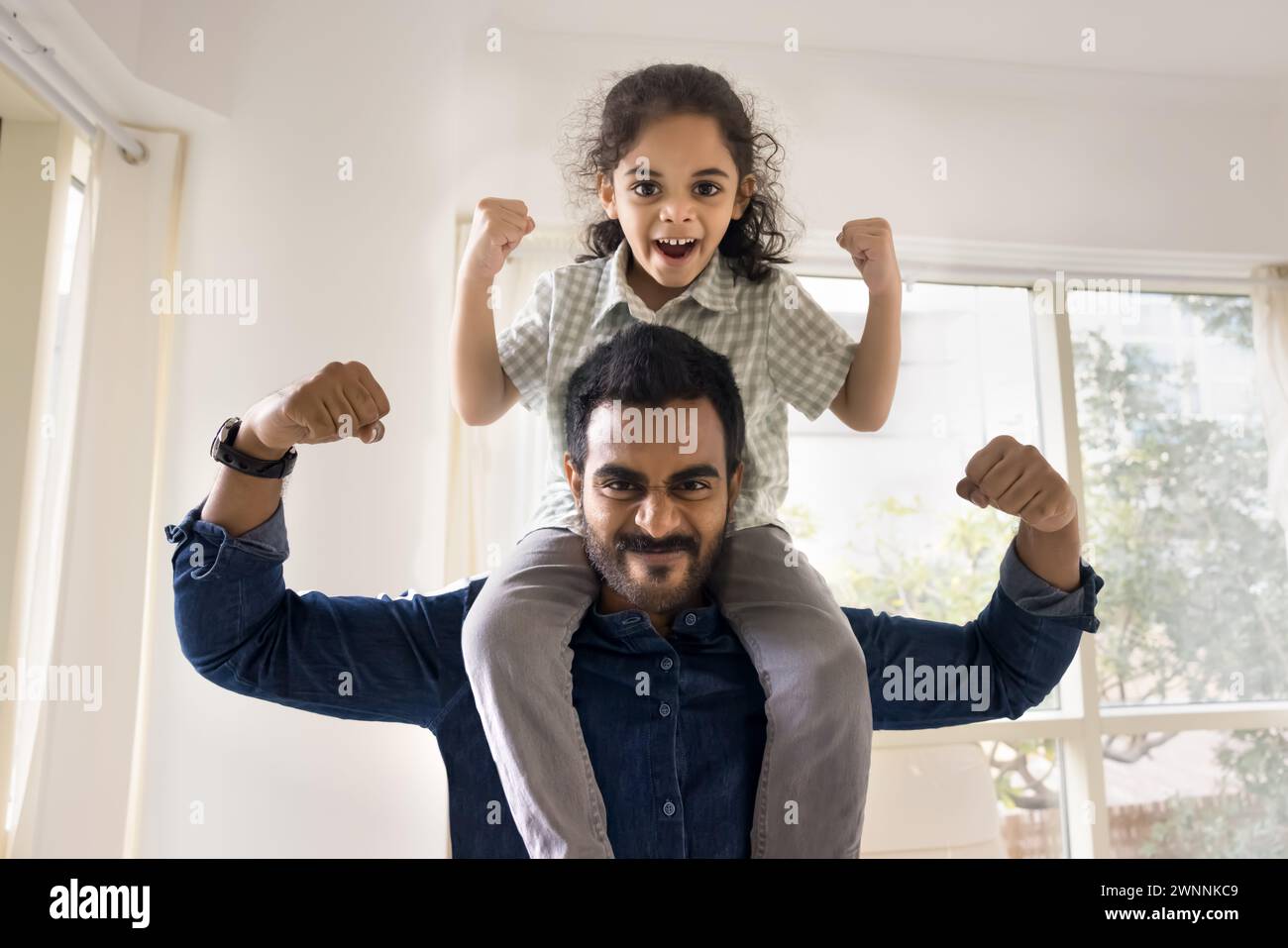 Cheerful strong Indian dad lifting little daughter kid on shoulders ...