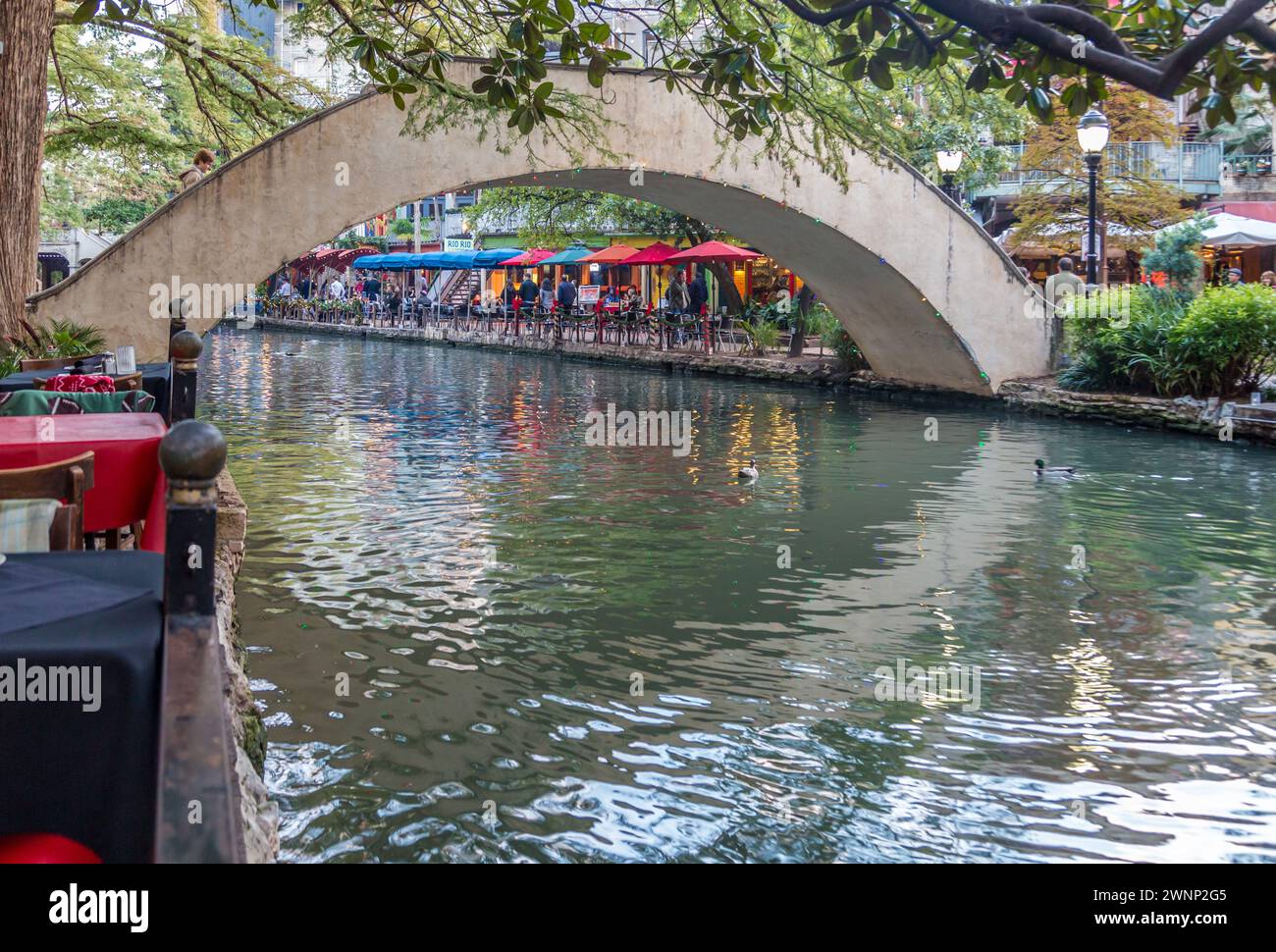 Colorful umbrellas on the sidewalk behind an arched bridge over the ...