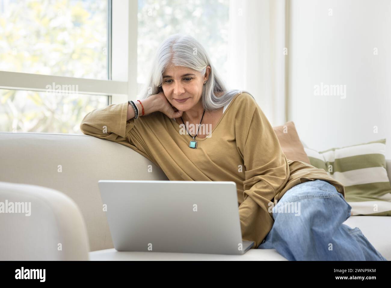 Positive gray haired older Hispanic woman relaxing with laptop Stock ...