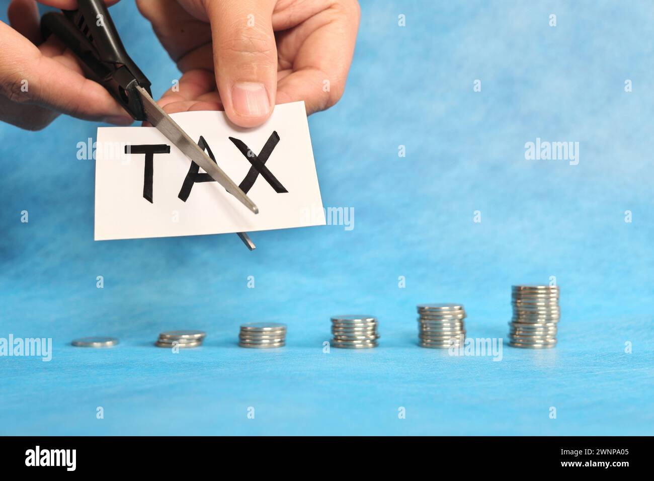 Tax cut concept. Hand cutting paper with scissor on blue background ...