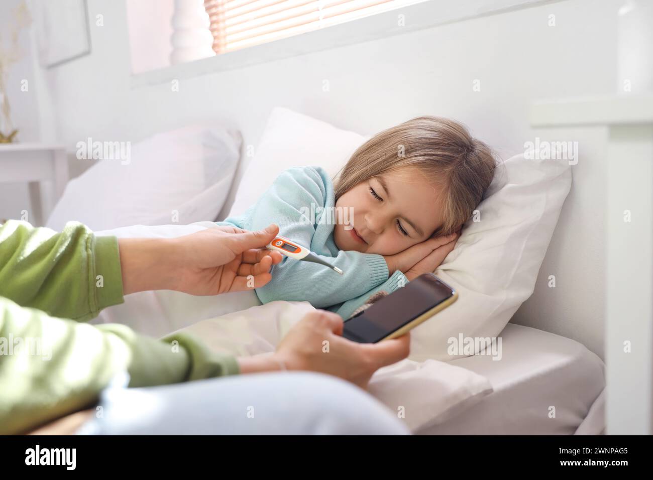 Sick little girl with her mother holding thermometer and mobile phone ...