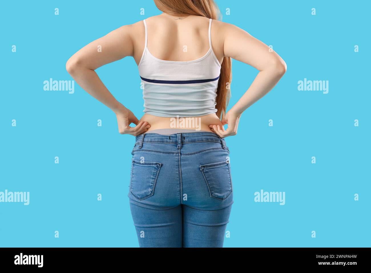 Young woman in tight jeans on blue background, back view. Weight gain ...