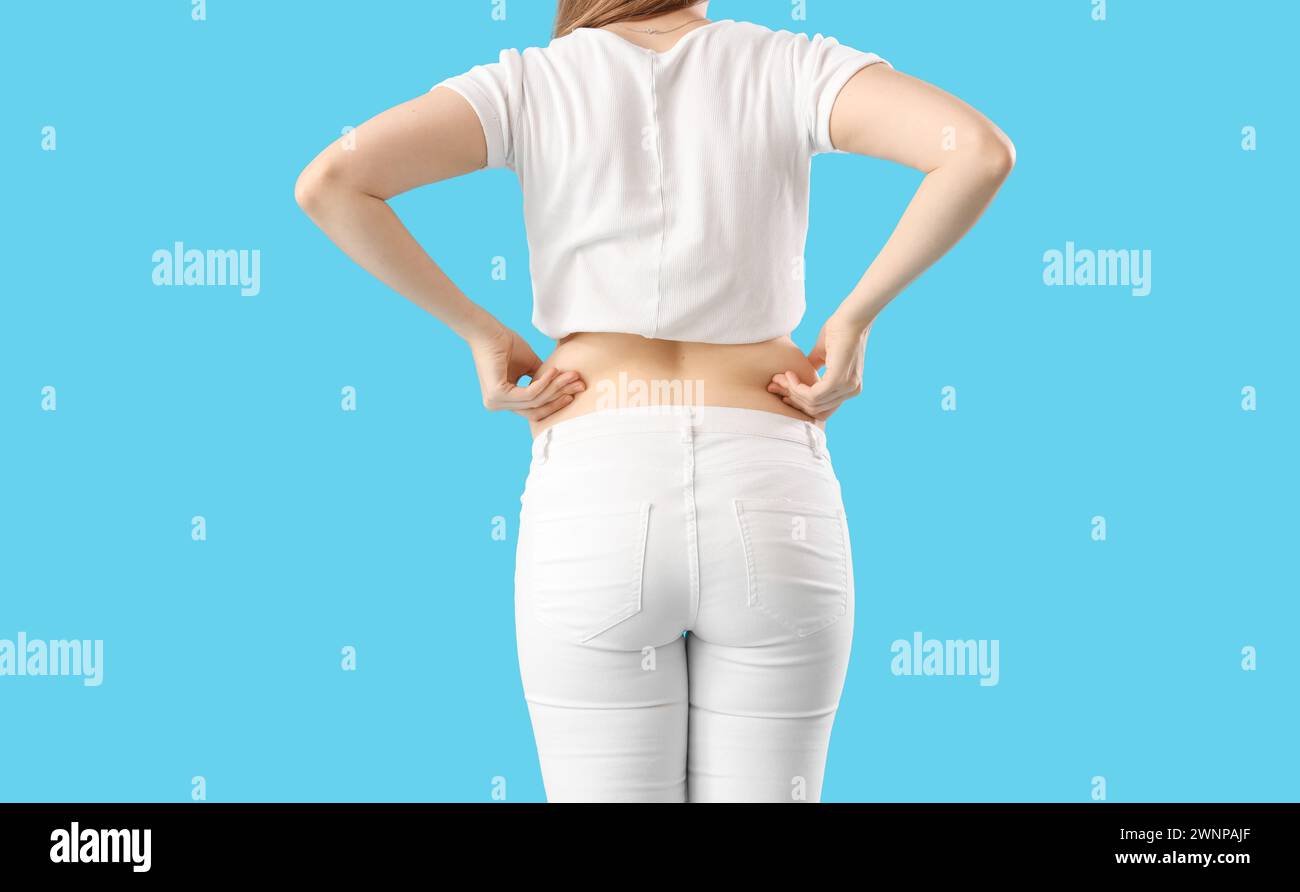 Young woman in tight pants on blue background, back view. Weight gain ...