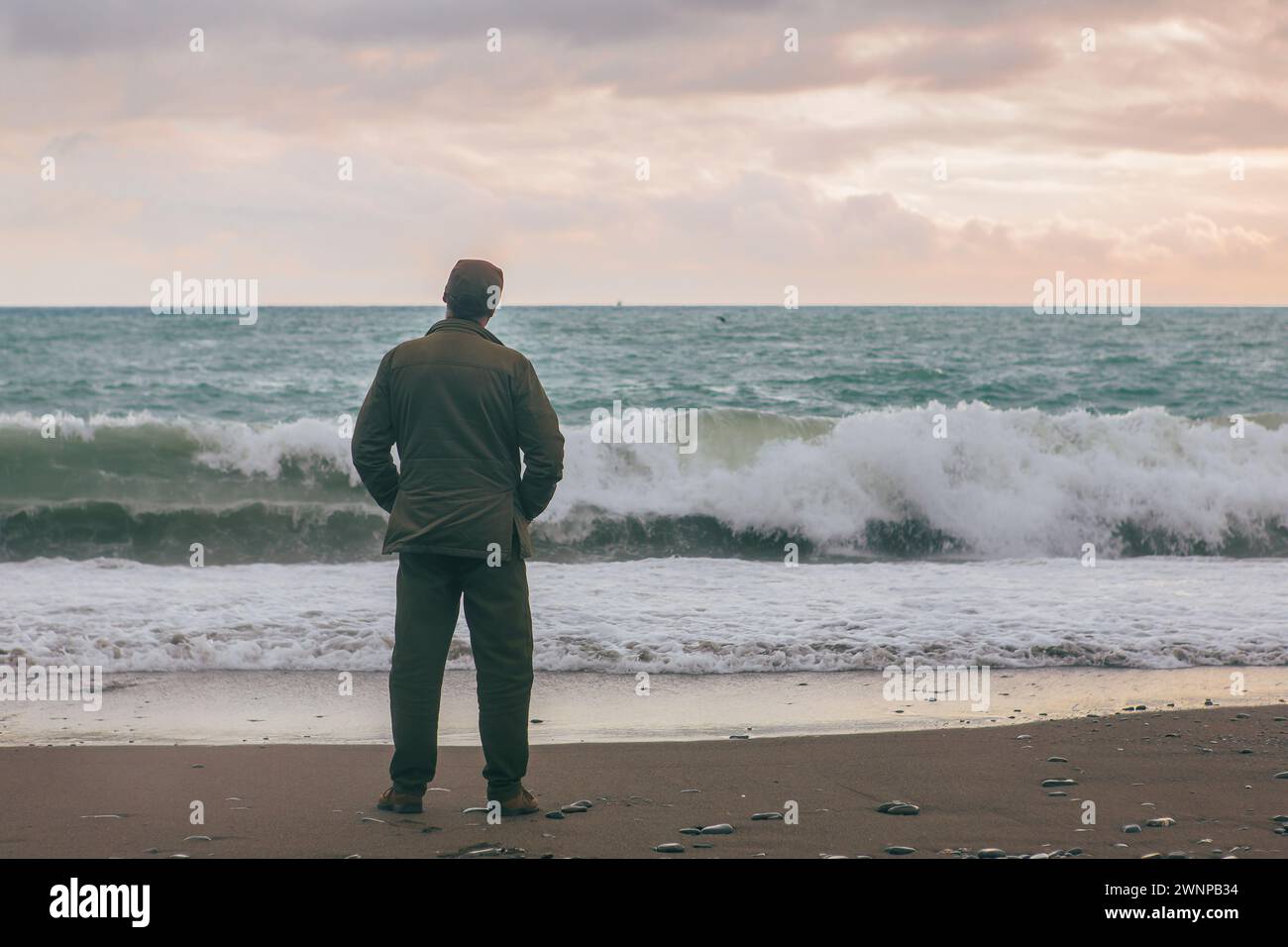 Solitary man standing by the seaside and staring in the distance. He's wearing a military outfit ...