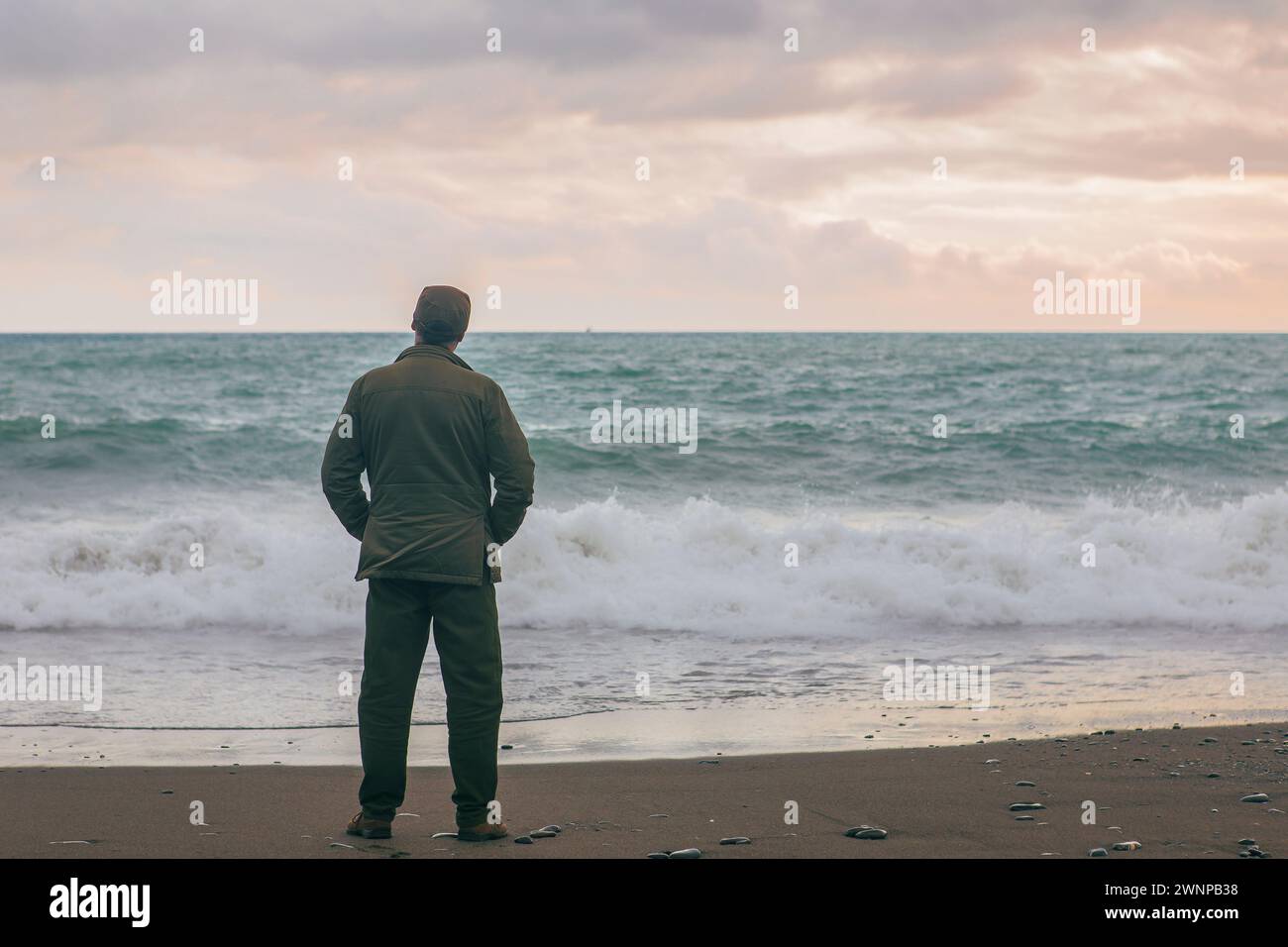 Solitary man standing by the seaside and staring in the distance. He's wearing a military outfit ...