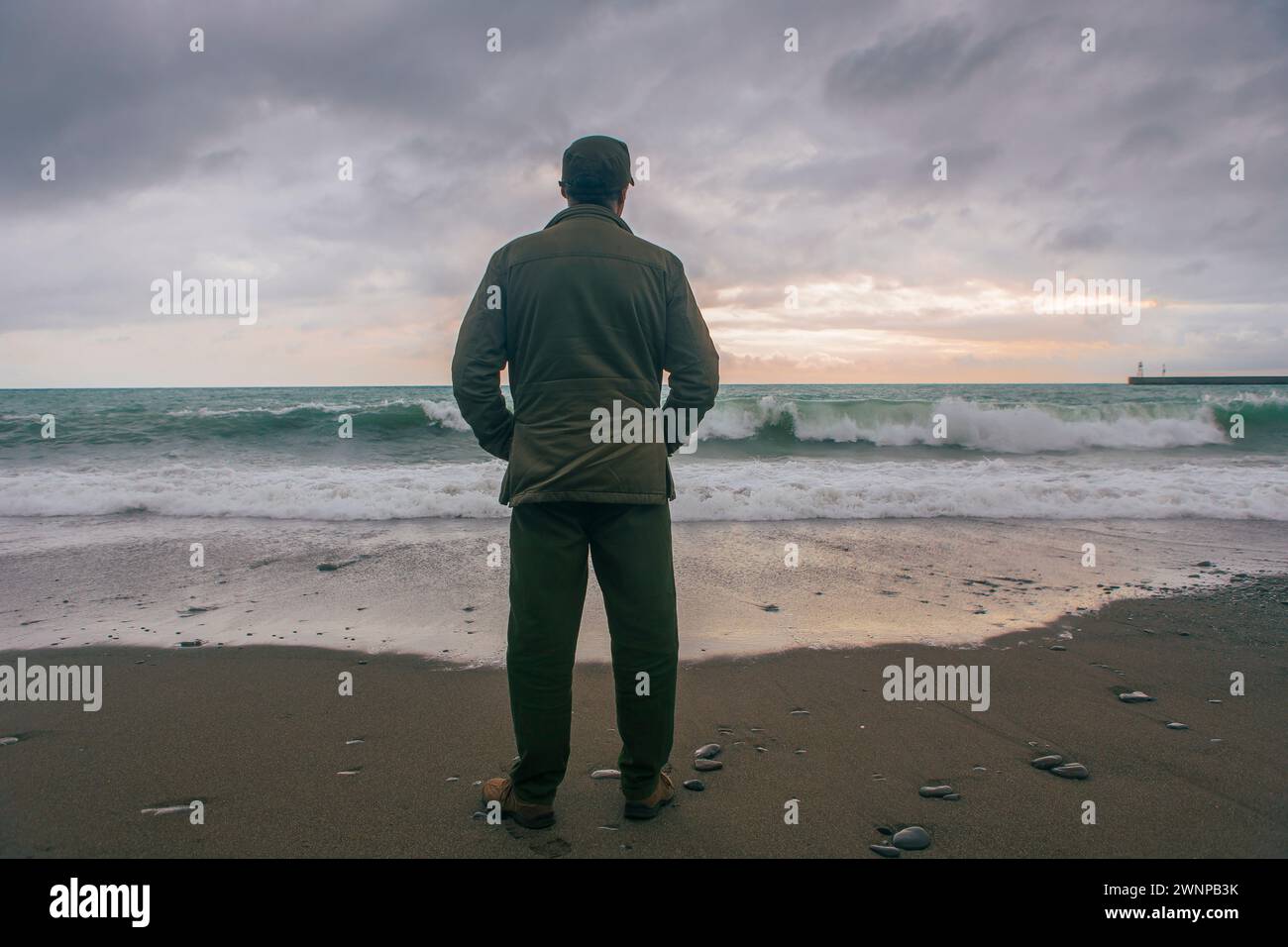 Solitary man standing by the seaside and staring in the distance. He's wearing a military outfit ...