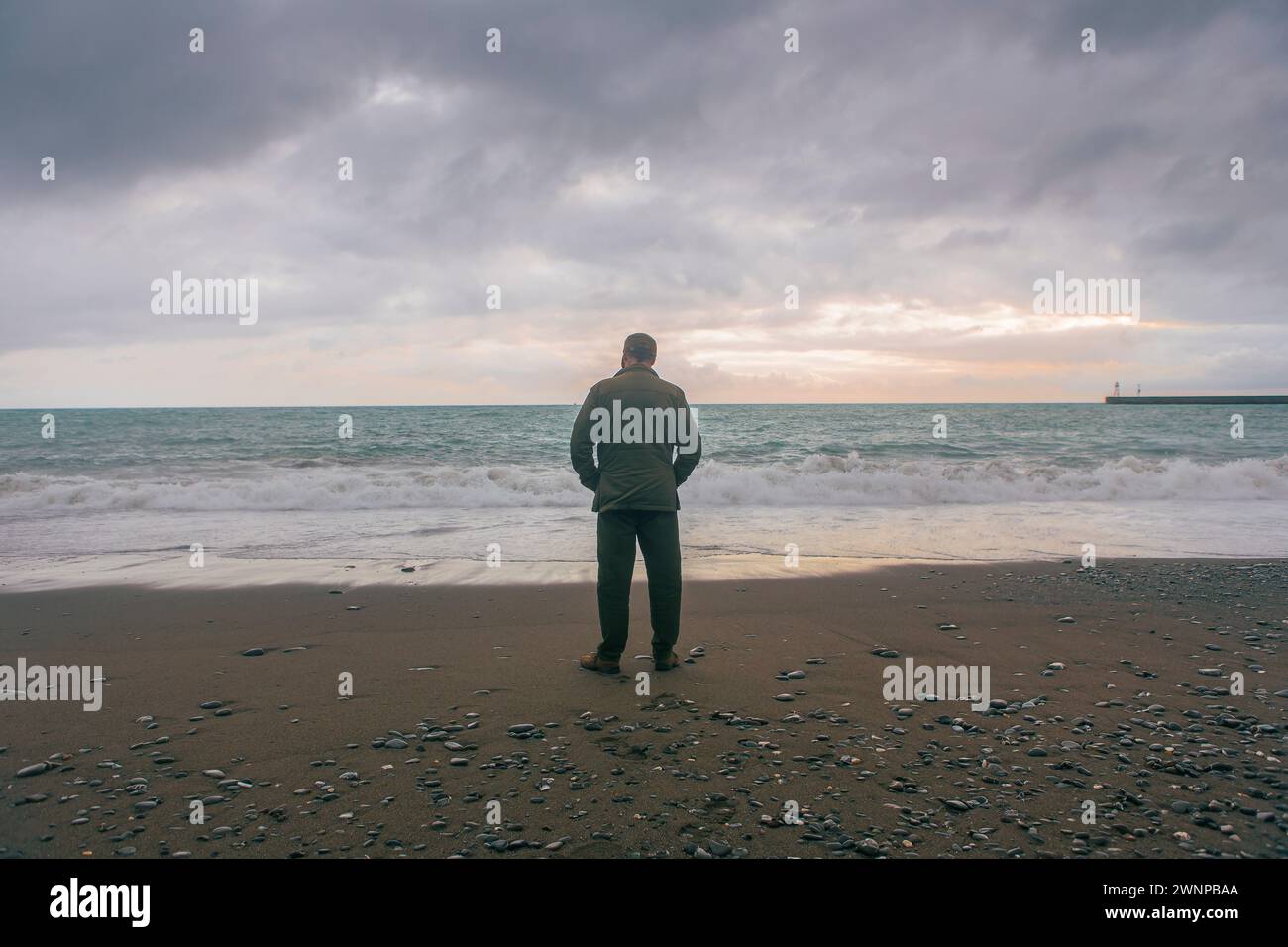 Solitary man standing by the seaside and staring in the distance. He's wearing a military outfit ...