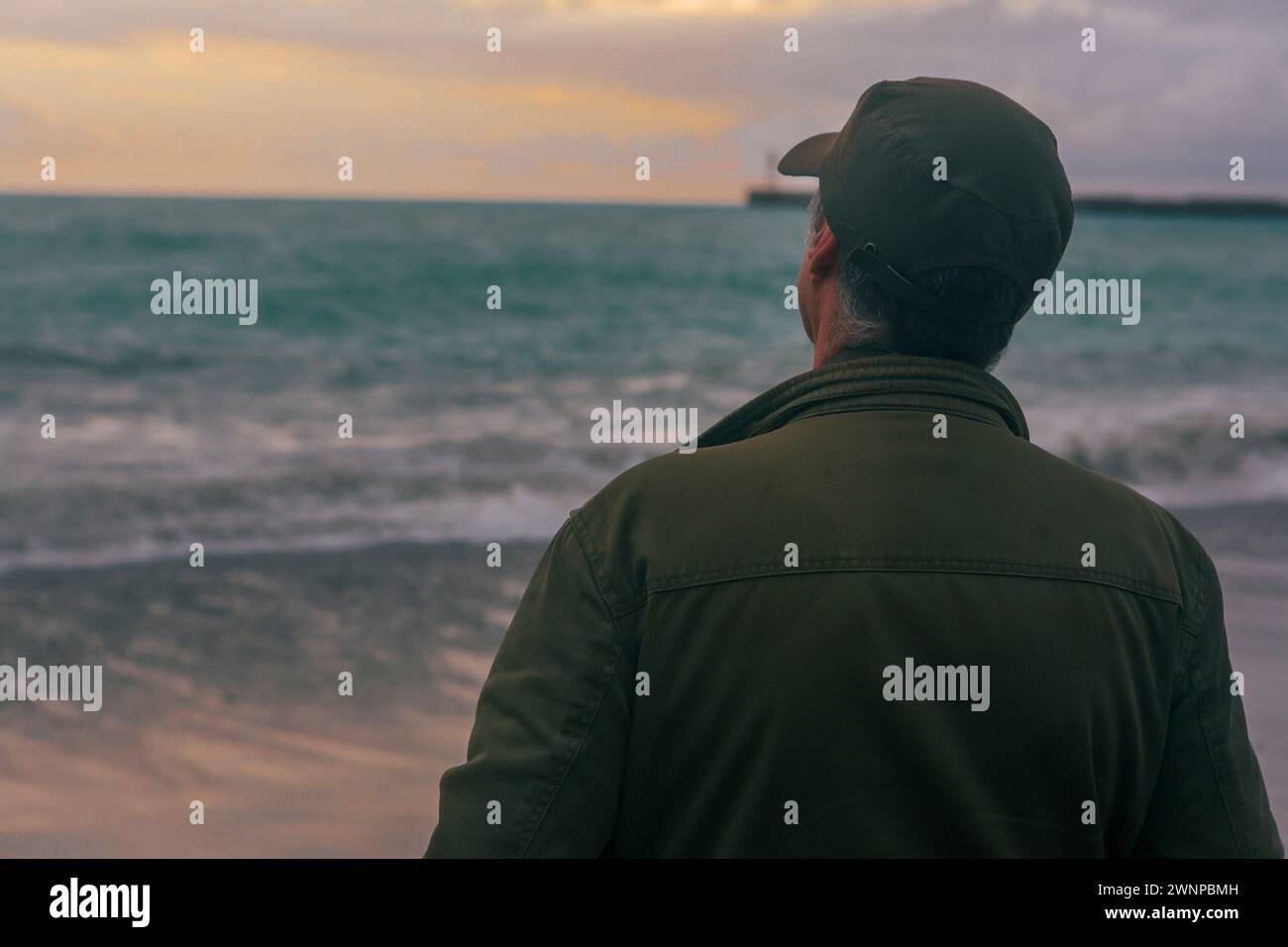 Solitary man standing by the seaside and staring in the distance. He's wearing a military outfit ...