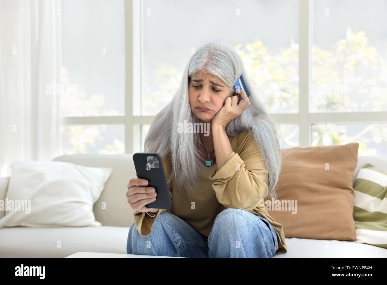 Sad elderly Hispanic woman looking at phone and credit card Stock Photo ...