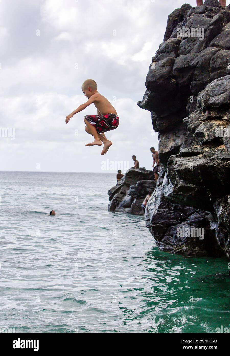 A young boy jumps from a large crop of rock into the water at Waimea ...