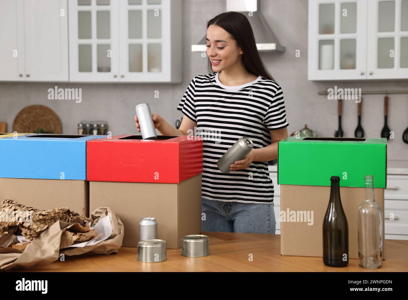 Garbage sorting. Smiling woman throwing metal can into cardboard box in ...