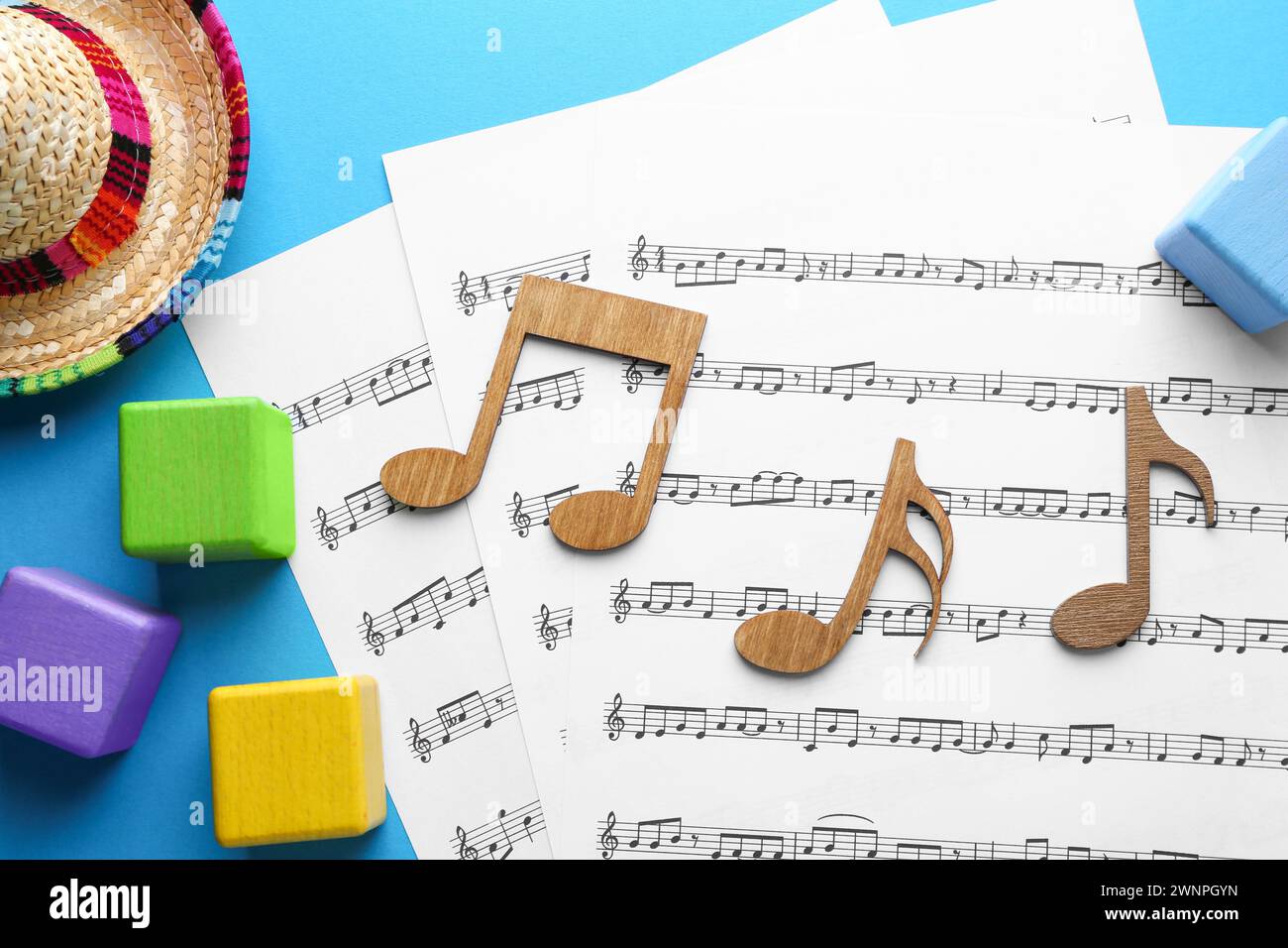 Baby songs. Music sheets, wooden notes, cubes and hat on light blue ...