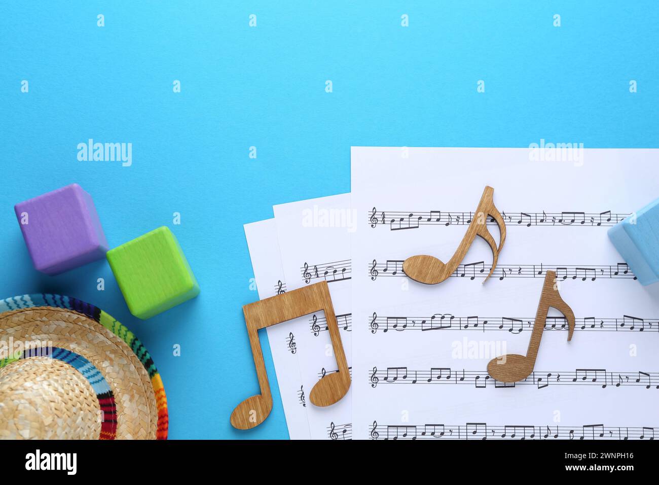 Baby songs. Music sheets, wooden notes, cubes and hat on light blue ...