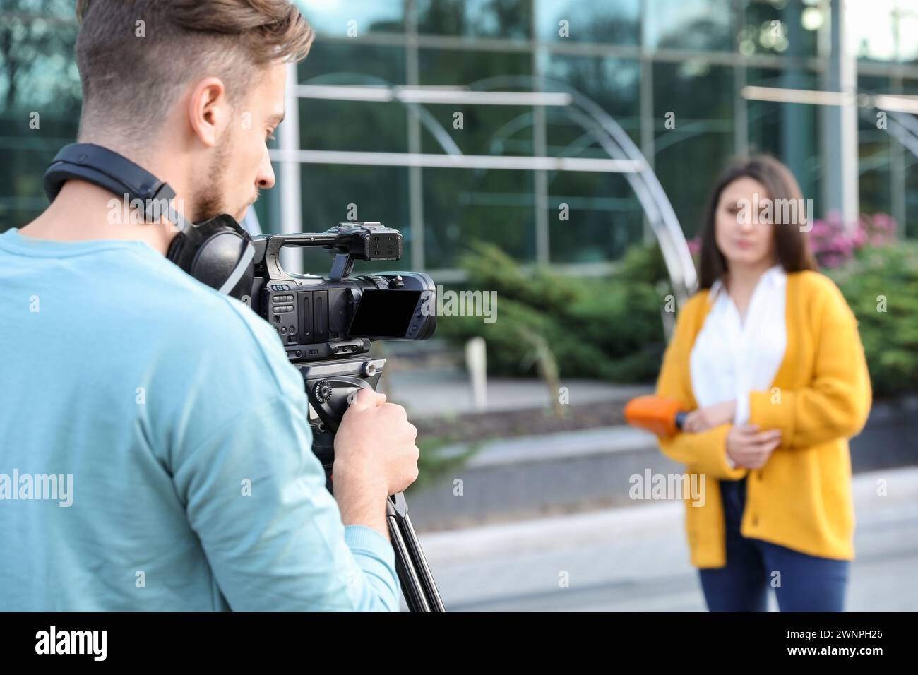 Young journalist and video operator working on city street. Space for ...