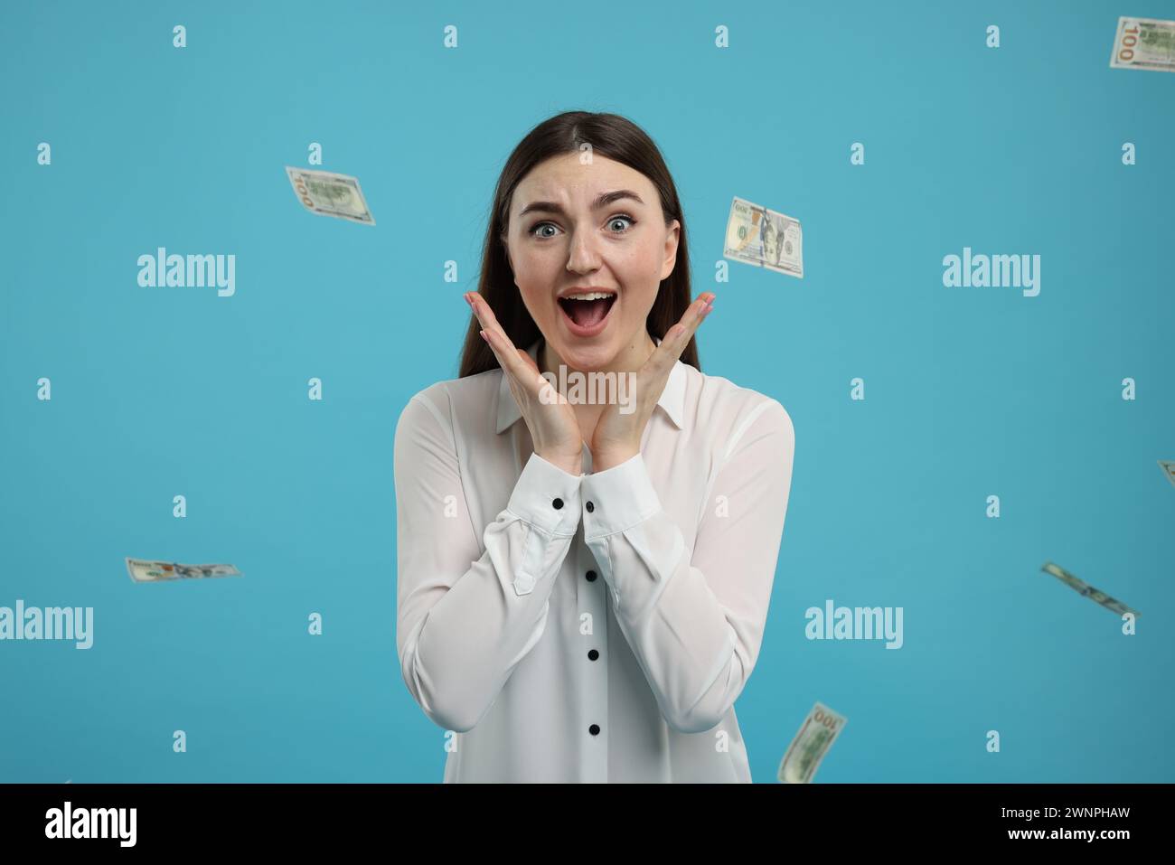 Excited woman under money shower on light blue background Stock Photo ...