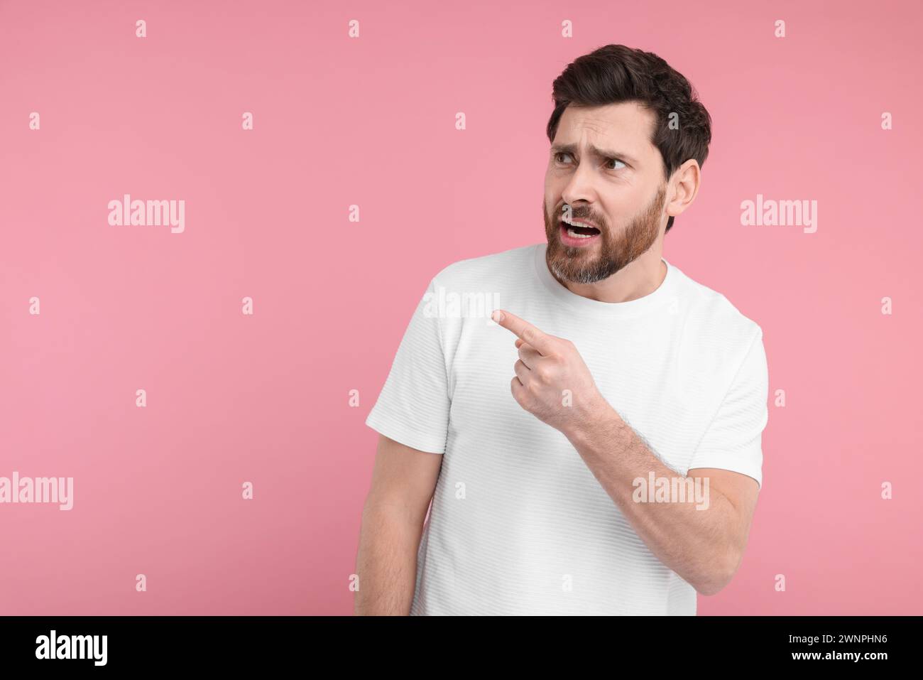 Surprised man pointing at something on pink background, space for text ...
