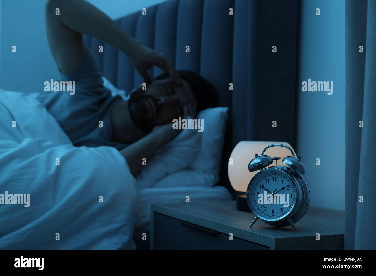 Man suffering from headache in bed at night, focus on alarm clock Stock ...