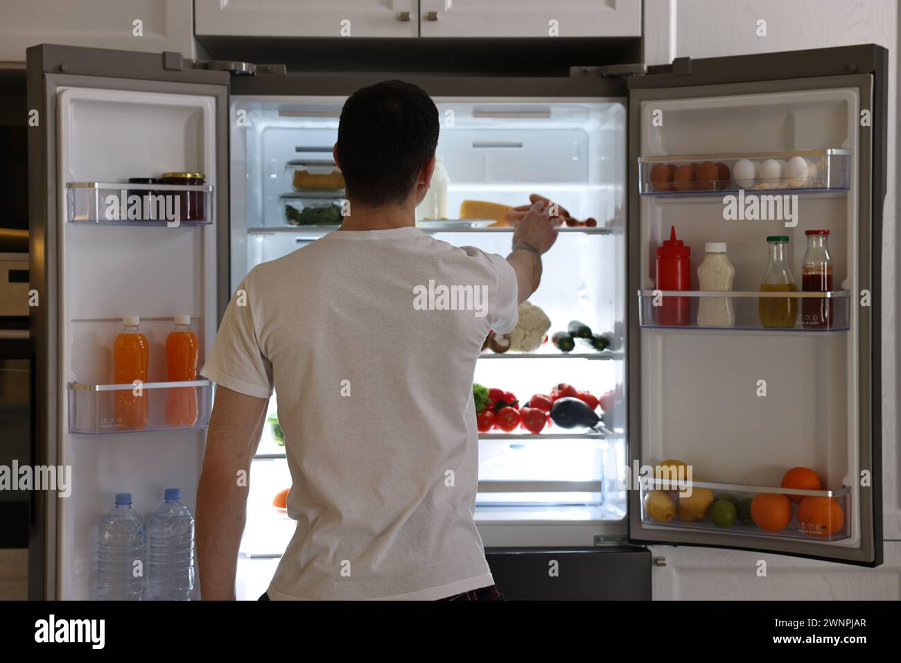 Man near refrigerator in kitchen, back view Stock Photo - Alamy