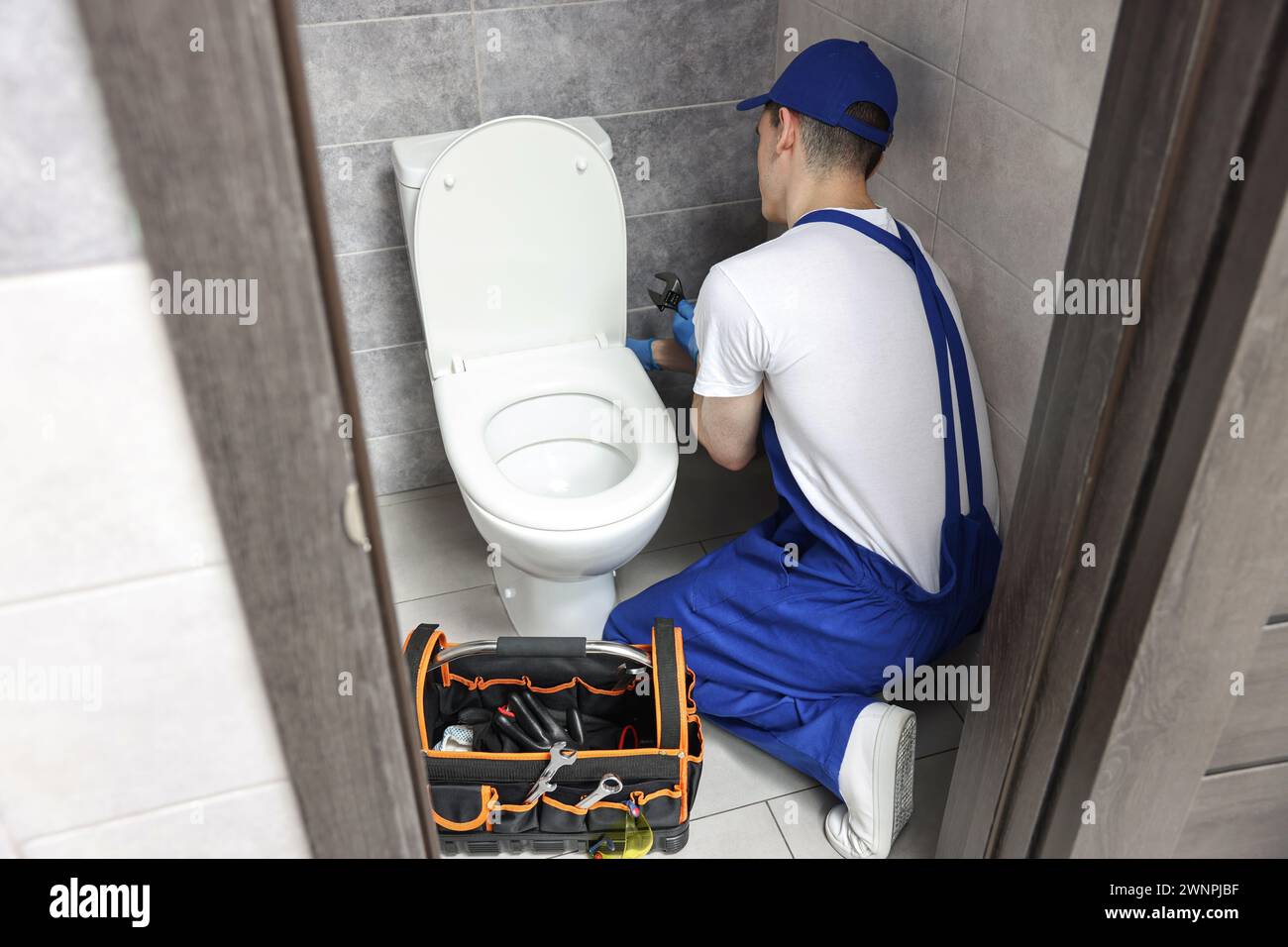 Plumber with spanner repairing toilet bowl in water closet Stock Photo ...