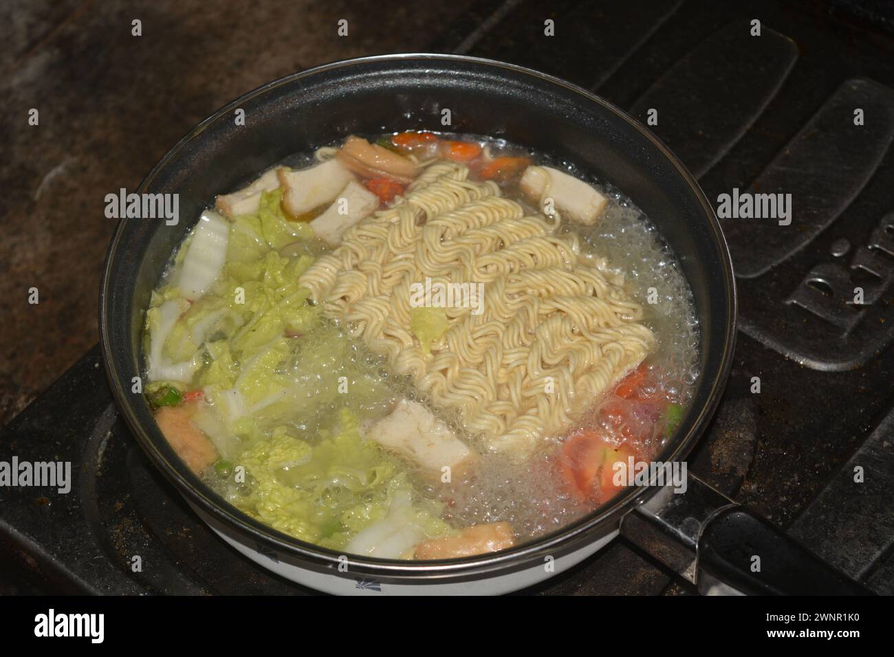 Photo of a pot of noodles being cooked with some vegetable toppings ...