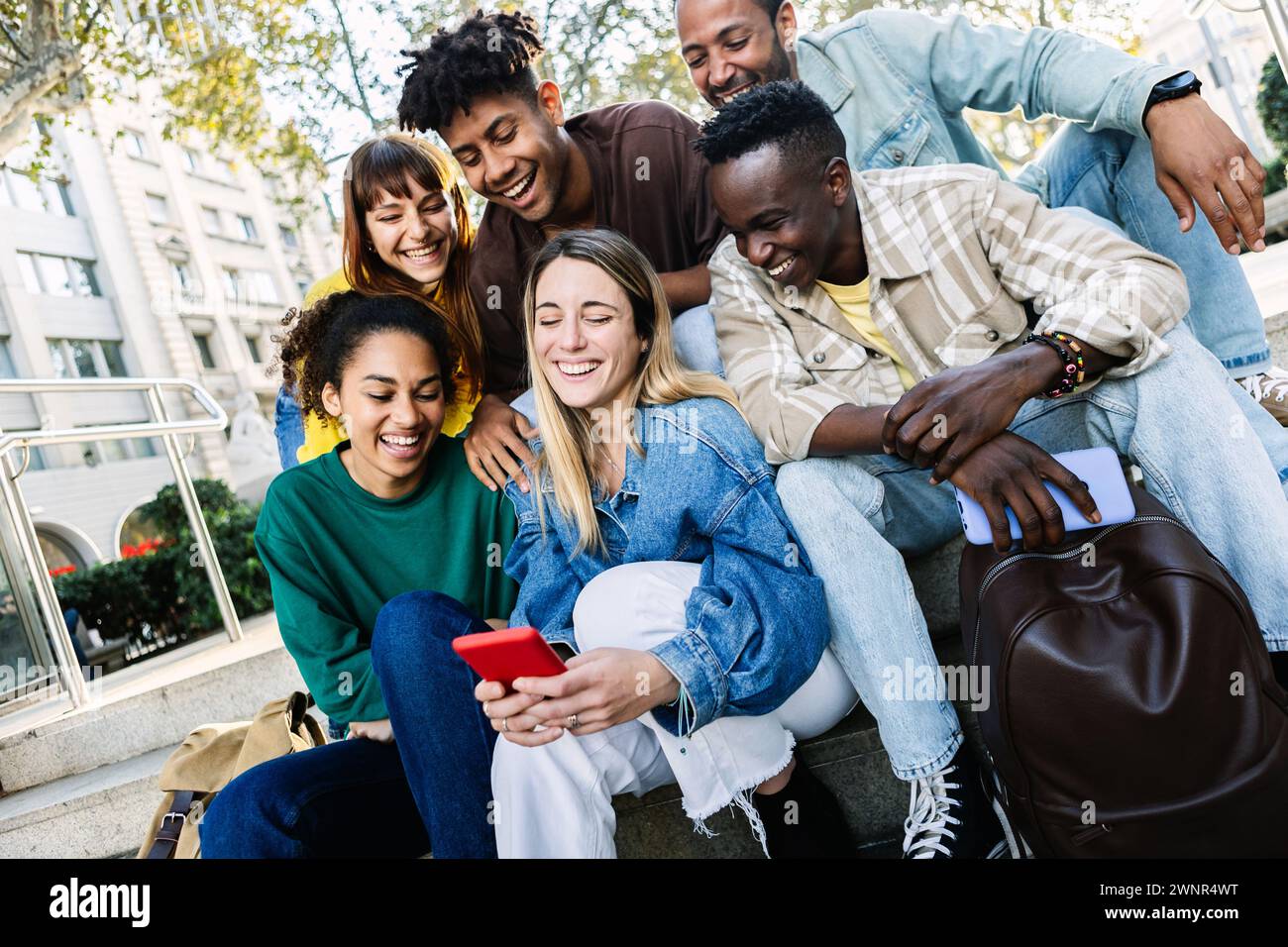 Diverse group of friends using mobile phone sitting at urban staircase ...