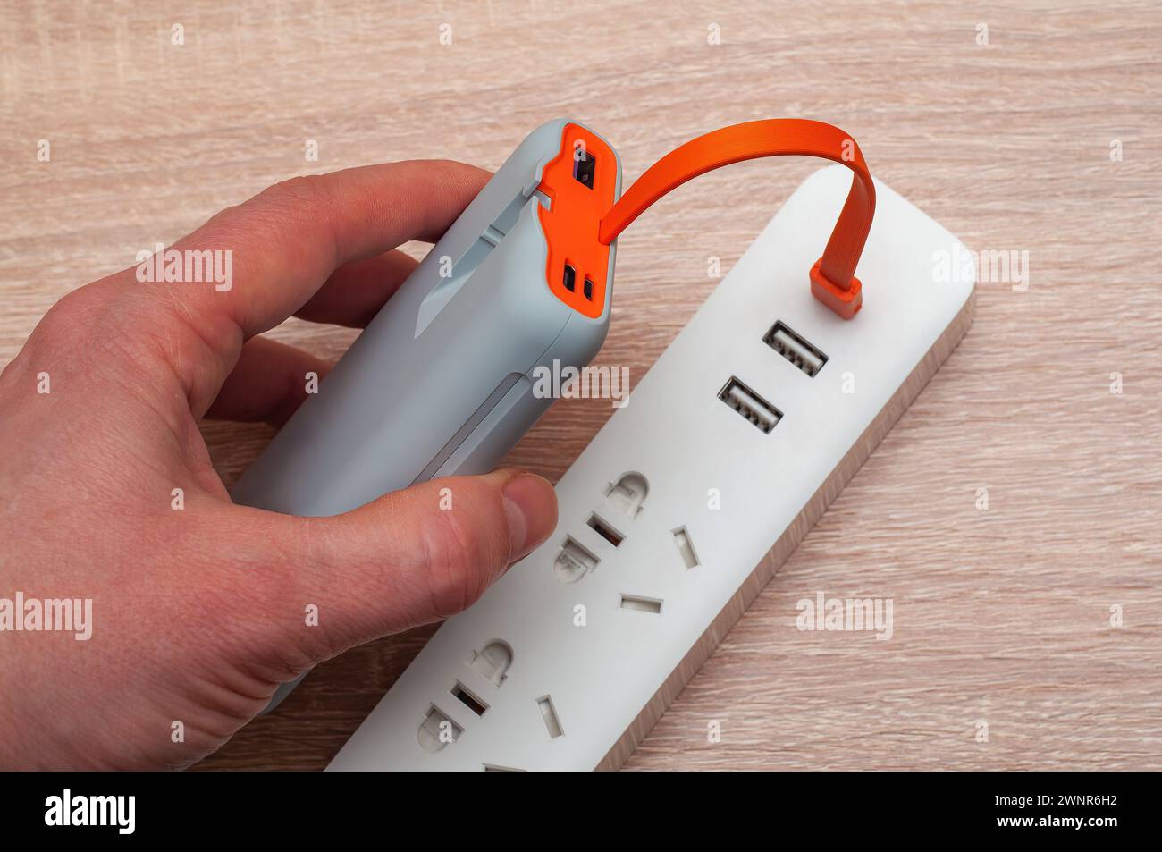 A hand holding a grey power bank connected via an orange USB cable to a ...