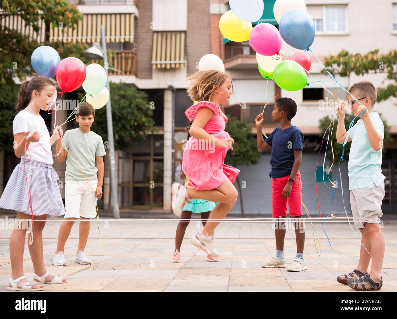 Cheerful preteen children with balloons playing chinese jump rope ...