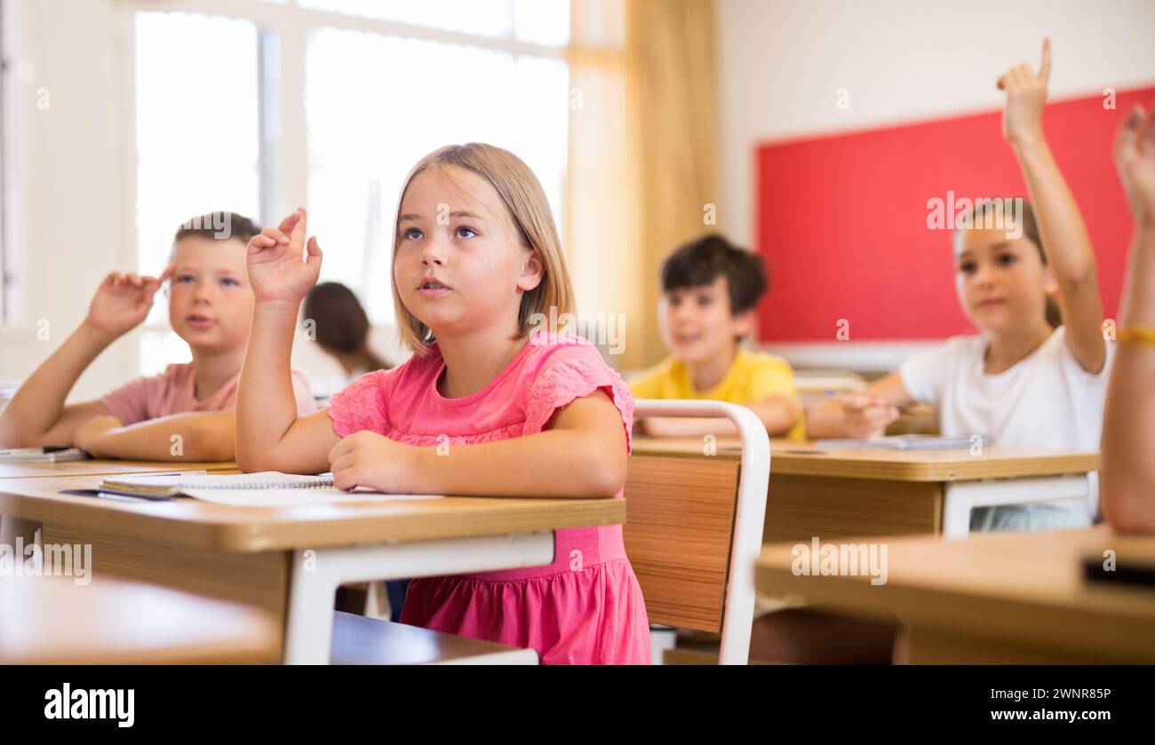 Girl raising hand to answer during lesson at classroom Stock Photo - Alamy