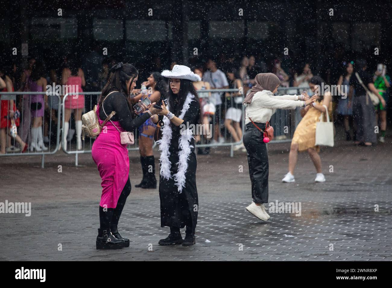3 March 2024. In the drizzle, female fans in the street taking picture ...