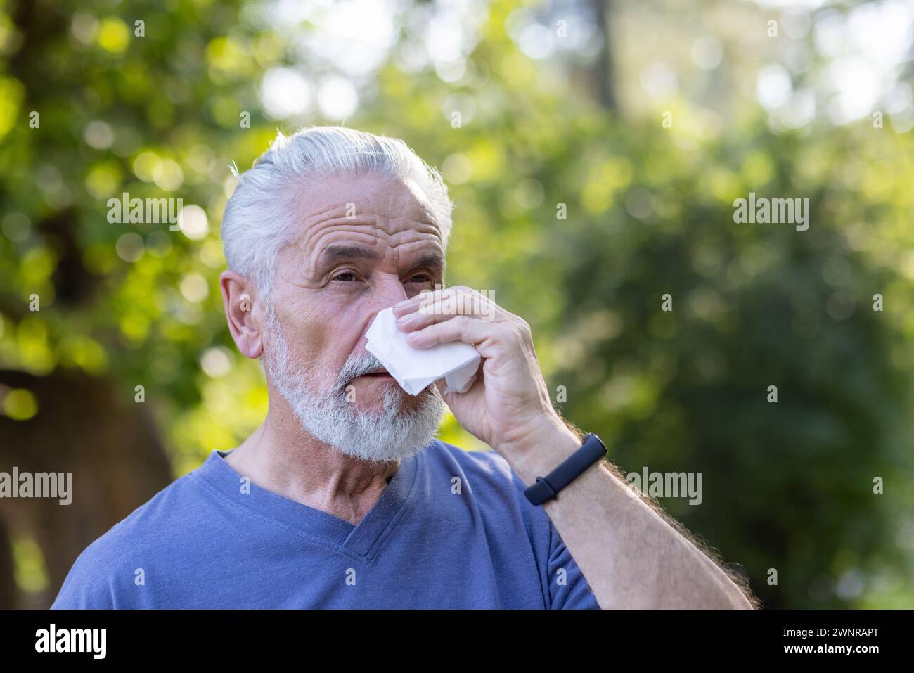 Close-up portrait of a sick elderly man with a beard standing in a park ...