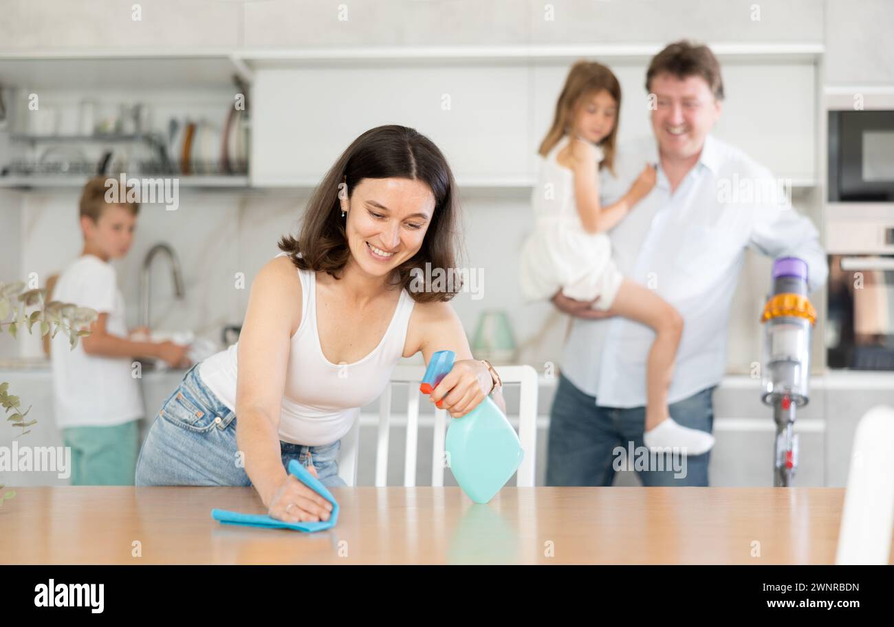 Wife cleans table with rag, husband and children clean kitchen in ...