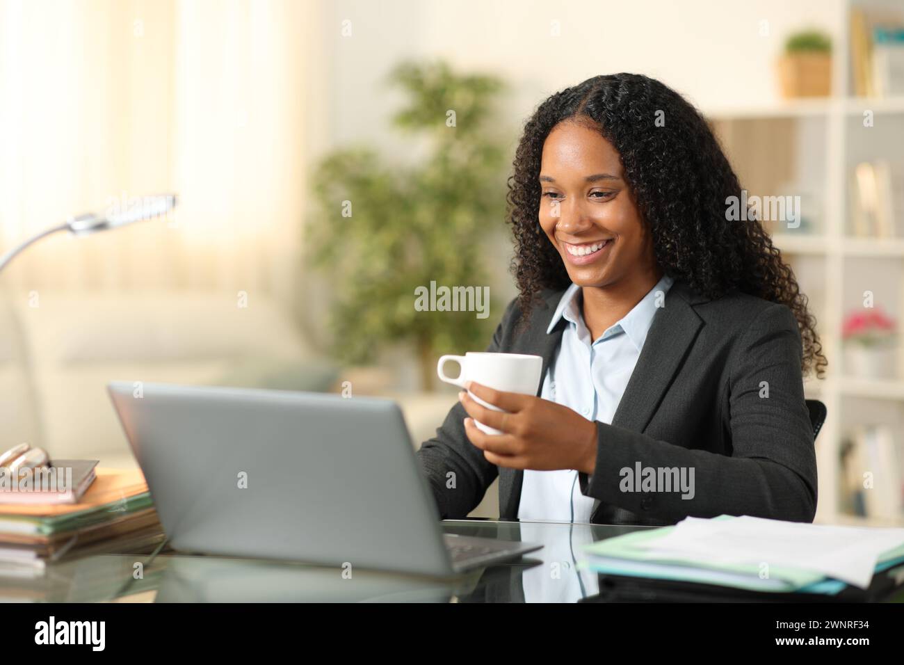 Happy black tele worker working online with a laptop and drinking ...