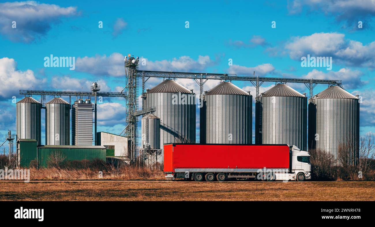 Semi-truck with red trailer in front of agricultural grain processing ...