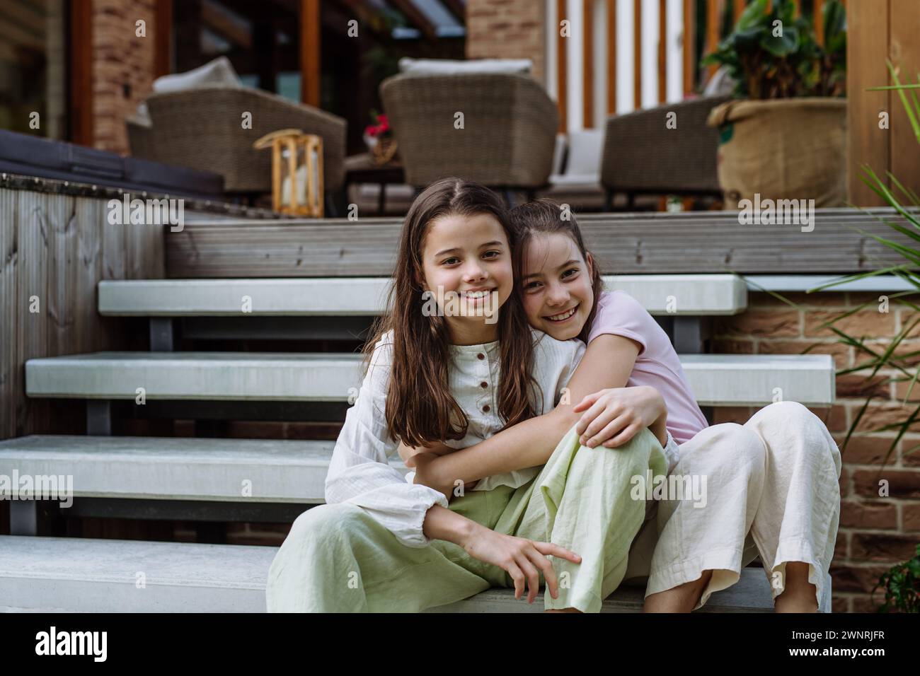Two sisters sitting on stairs in front of house, embracing. Sisterly ...