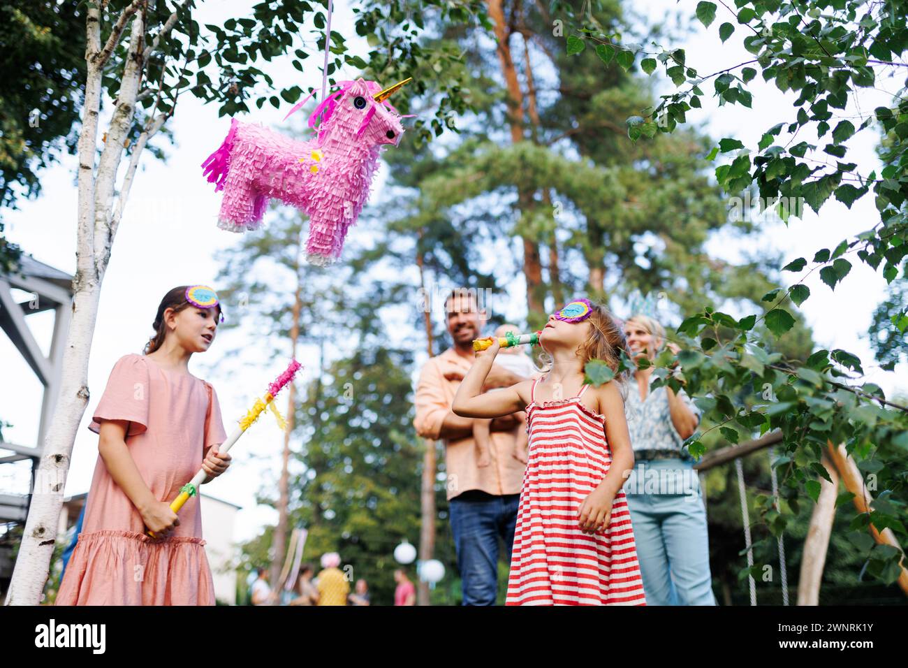 Two girls smashing, hitting pinata with a stick at birthday party ...