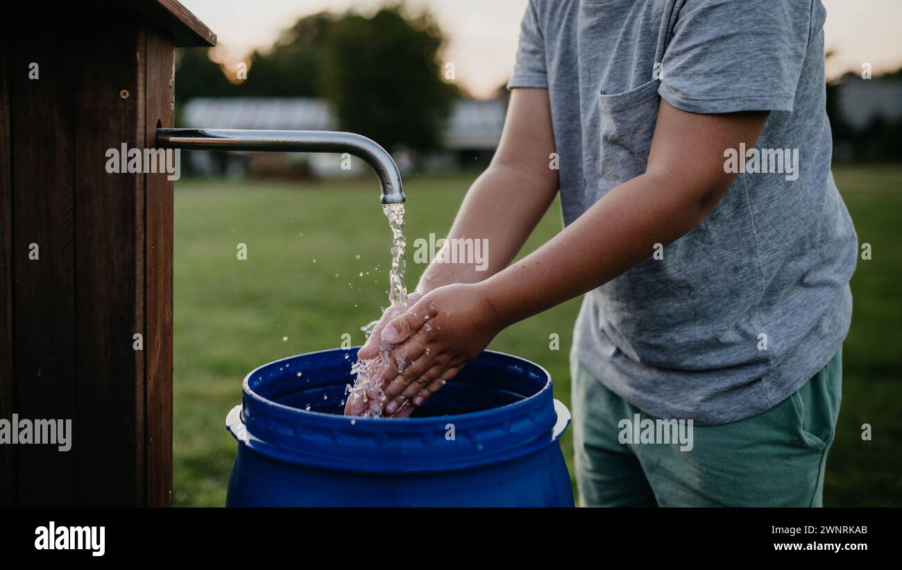Boy washing his hands with water from a well. Well with a pump for ...