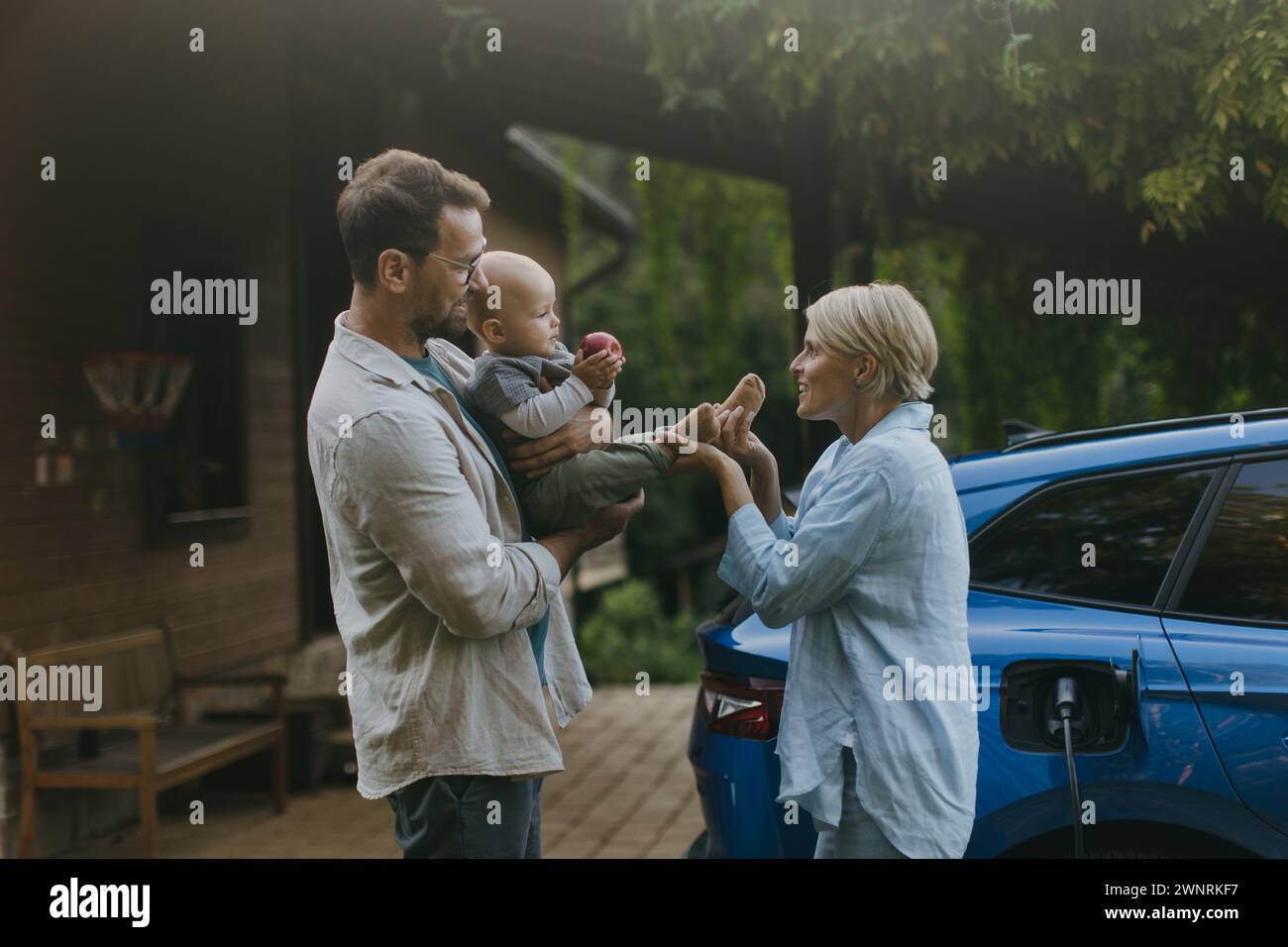 Young family with baby standing by their electric car. Electric vehicle ...