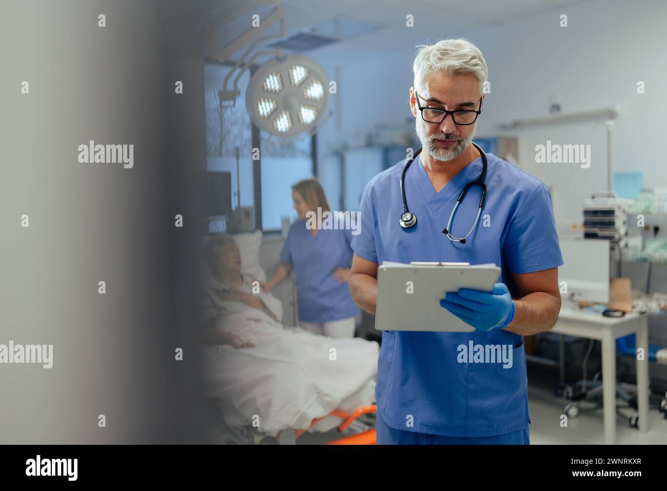 Portrait of handsome male doctor, patient in hospital bed behind. ER ...