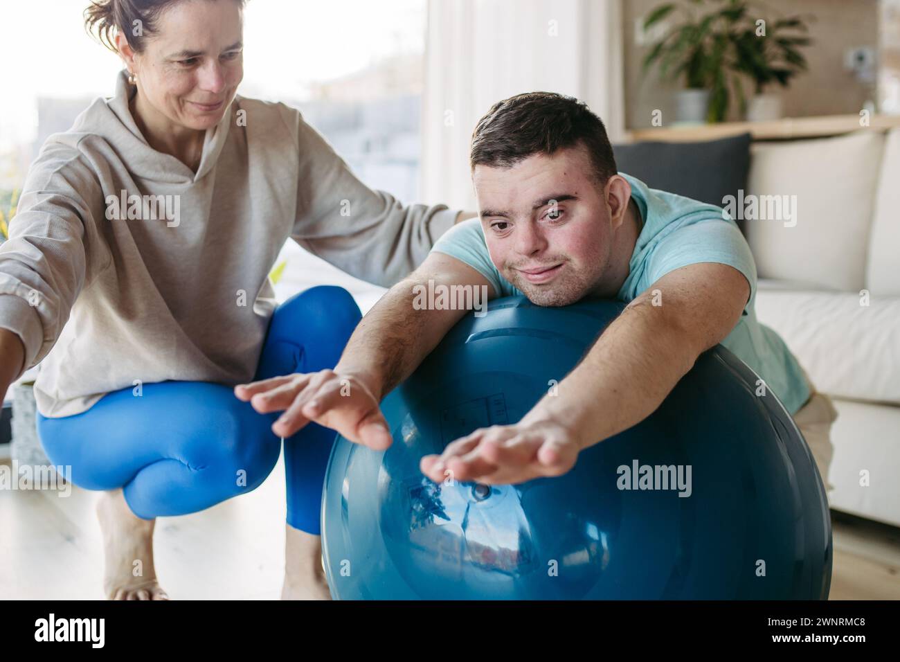 Young man with Down syndrome exercising at home with his mother on ...