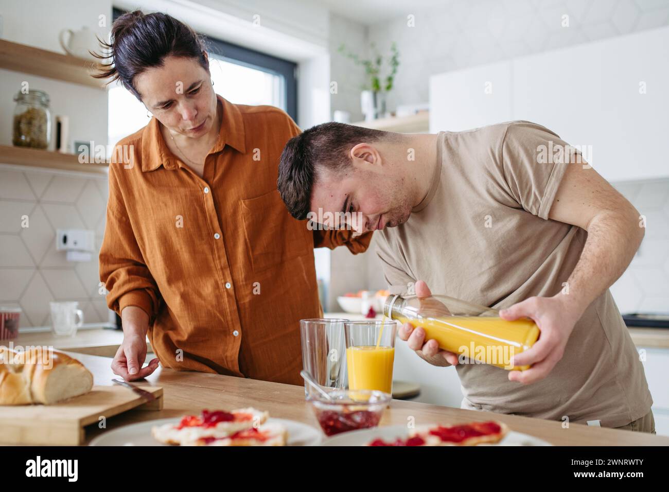 Young man with Down syndrome, pouring juice, preparing breakfast with ...