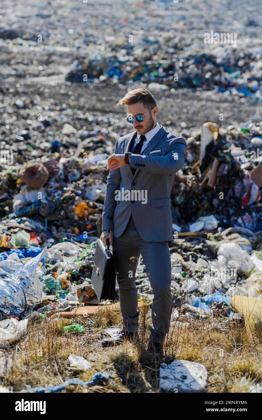 Businessman looking at watch, checking time standing on landfill, large ...