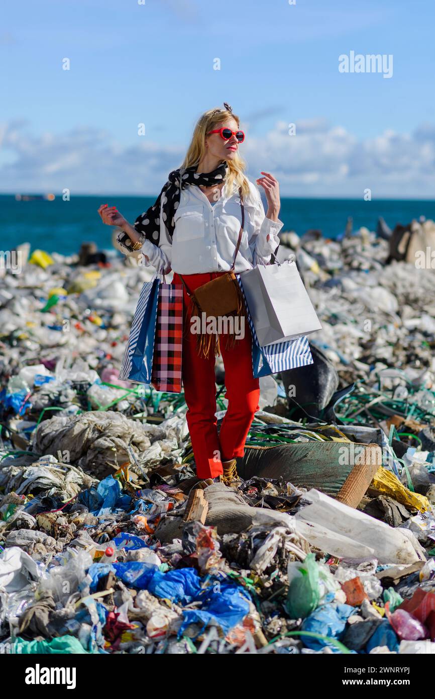 Modern woman on landfill with shopping bags. standing on pile of waste ...