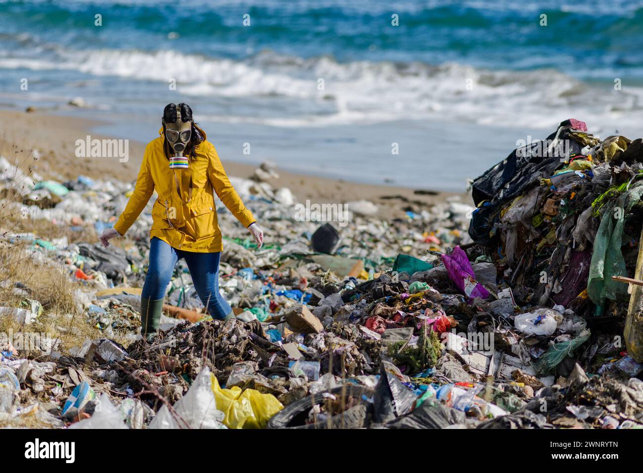 Activist with gas mask standing on landfill, large pile of waste by sea ...