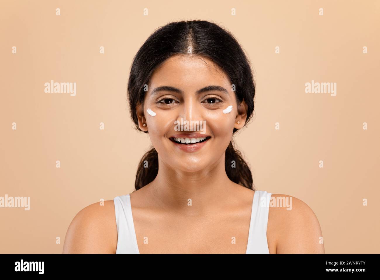 Portrait of cheerful young indian woman with white cream spots on face ...
